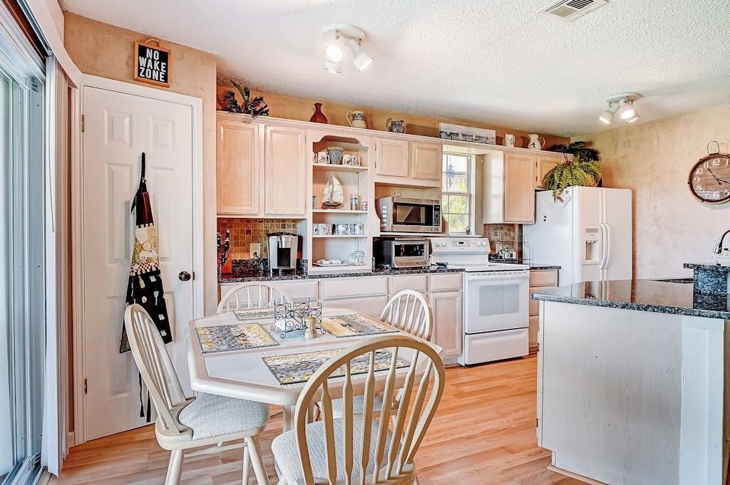 Uma cozinha com armários brancos, uma mesa de jantar com cadeiras, um relógio na parede e uma placa com a inscrição 'NO WAKE ZONE'.