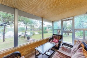 Um alpendre coberto com móveis de vime, janelas amplas e vista para um jardim.