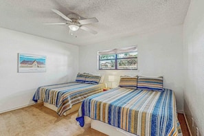 Quarto com duas camas, um ventilador de teto, janela com persianas e um quadro na parede.