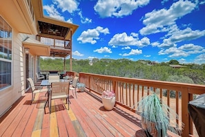 Um deck de madeira com mobiliário para área externa, uma área coberta com ventilador de teto e vista para uma paisagem verde.