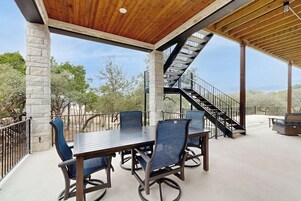 Um pátio externo com mesa e cadeiras, uma escadaria e vista da paisagem ao redor.