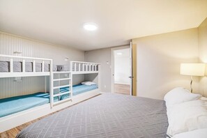 Quarto com beliches, uma cama de solteiro, uma luminária e uma porta que dá para outro cômodo.