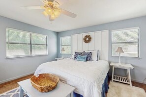 Um quarto com cama, ventoinha no teto, grinalda na parede e mesa de cabeceira com abajur.