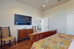 Quarto com cama, televisão na parede, um banco de madeira e porta para outro cômodo.