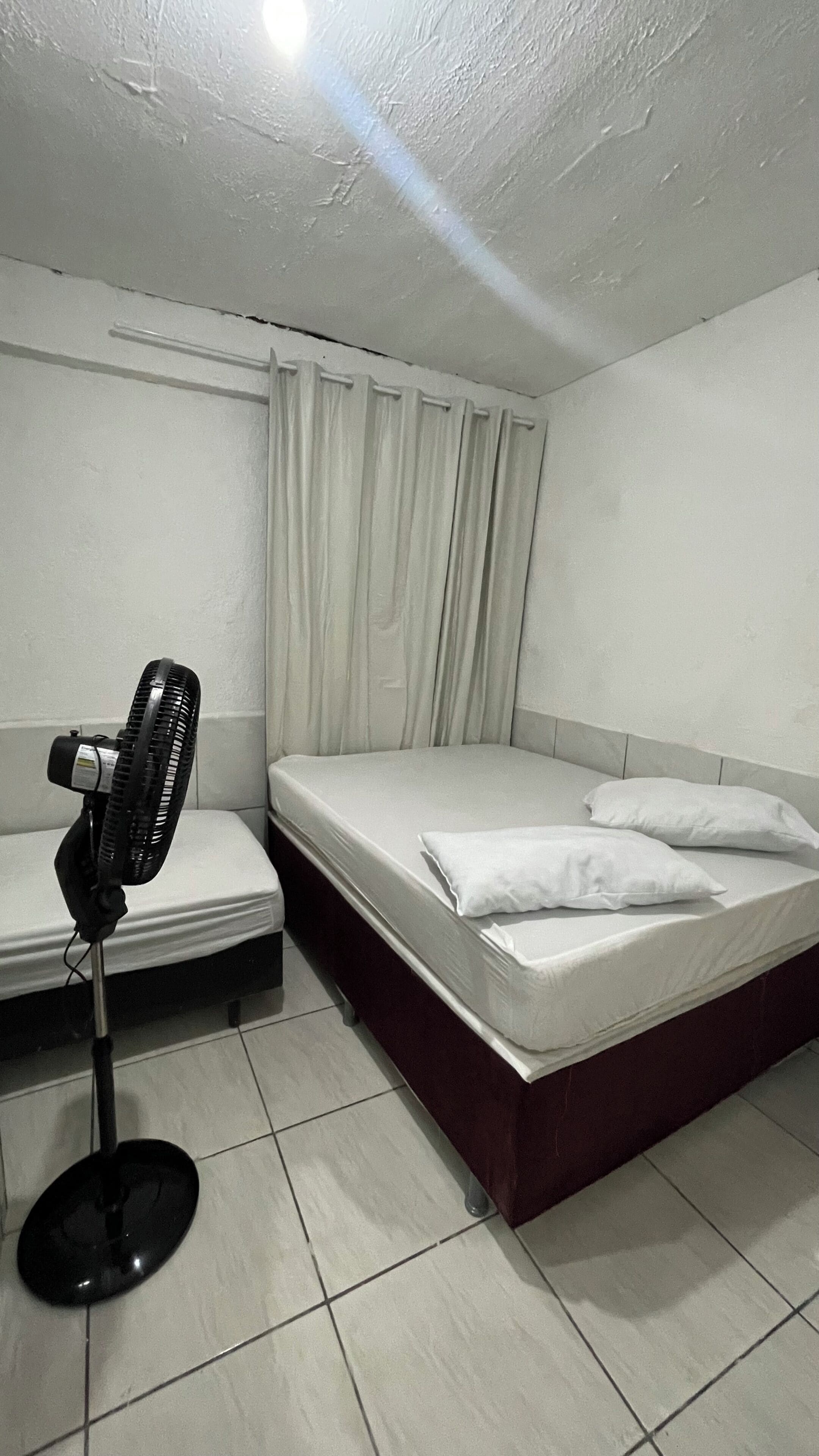 Quarto com cama, ventilador e cortina.
