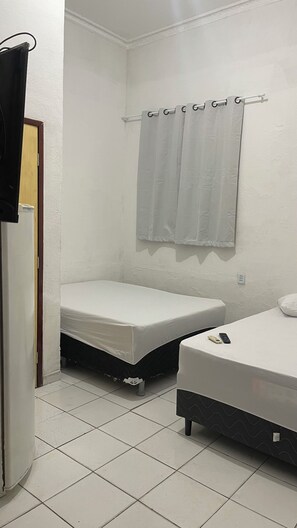 Quarto pequeno e compacto com duas camas, sanitário e chuveiro.