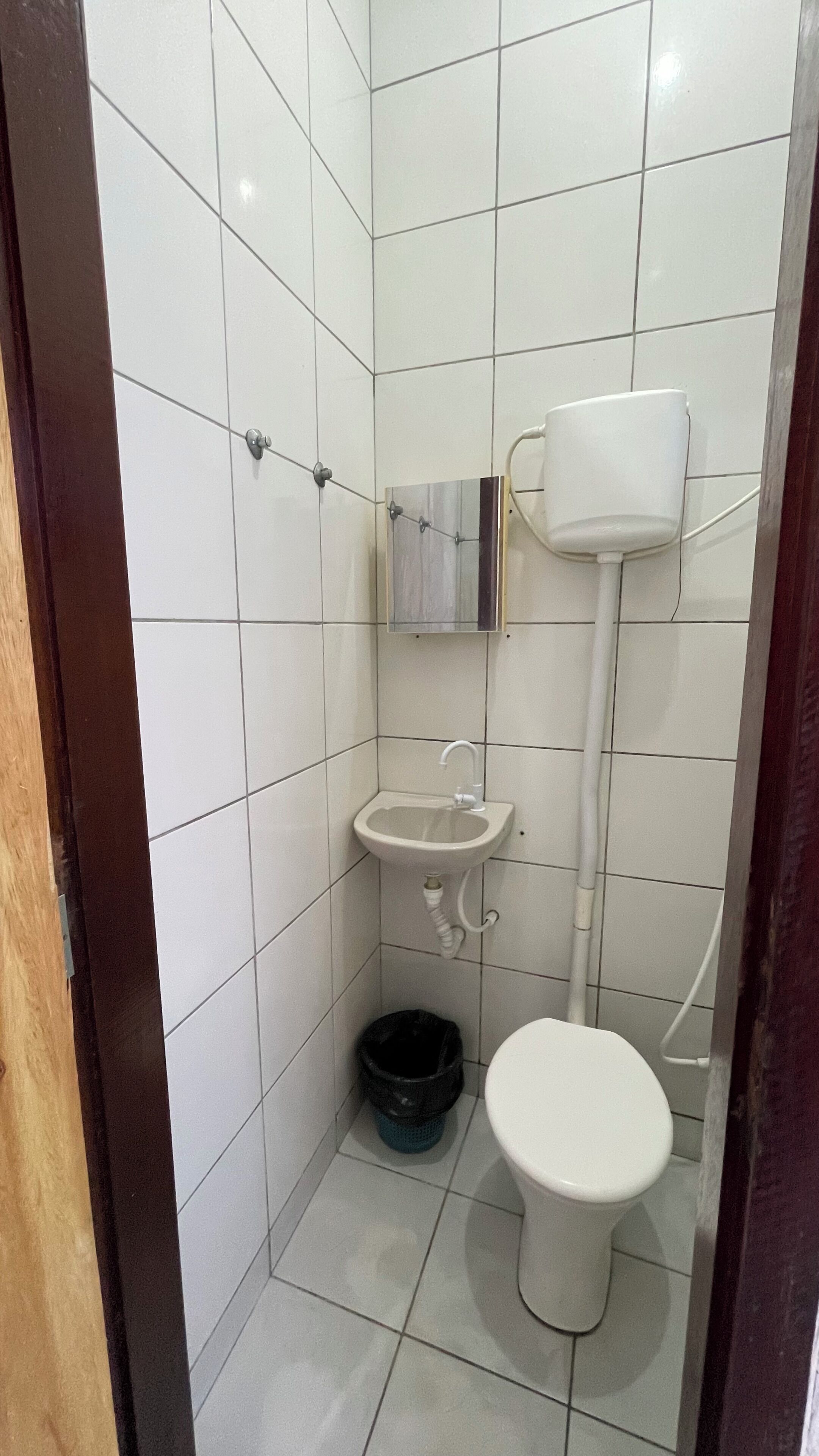 Uma casa de banho pequena, com azulejos, com sanita, lavatório e rolo de papel higiénico fixado na parede.