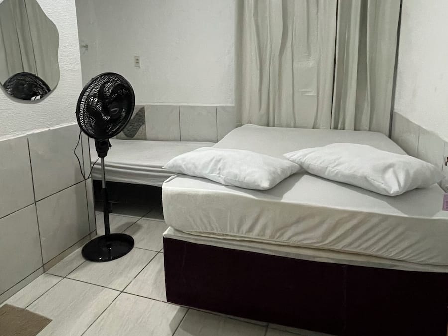 Um quarto com uma cama, um ventilador, uma luminária no teto e um espelho na parede.