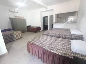 Quarto com três camas, um guarda-roupa e uma pequena mesa.