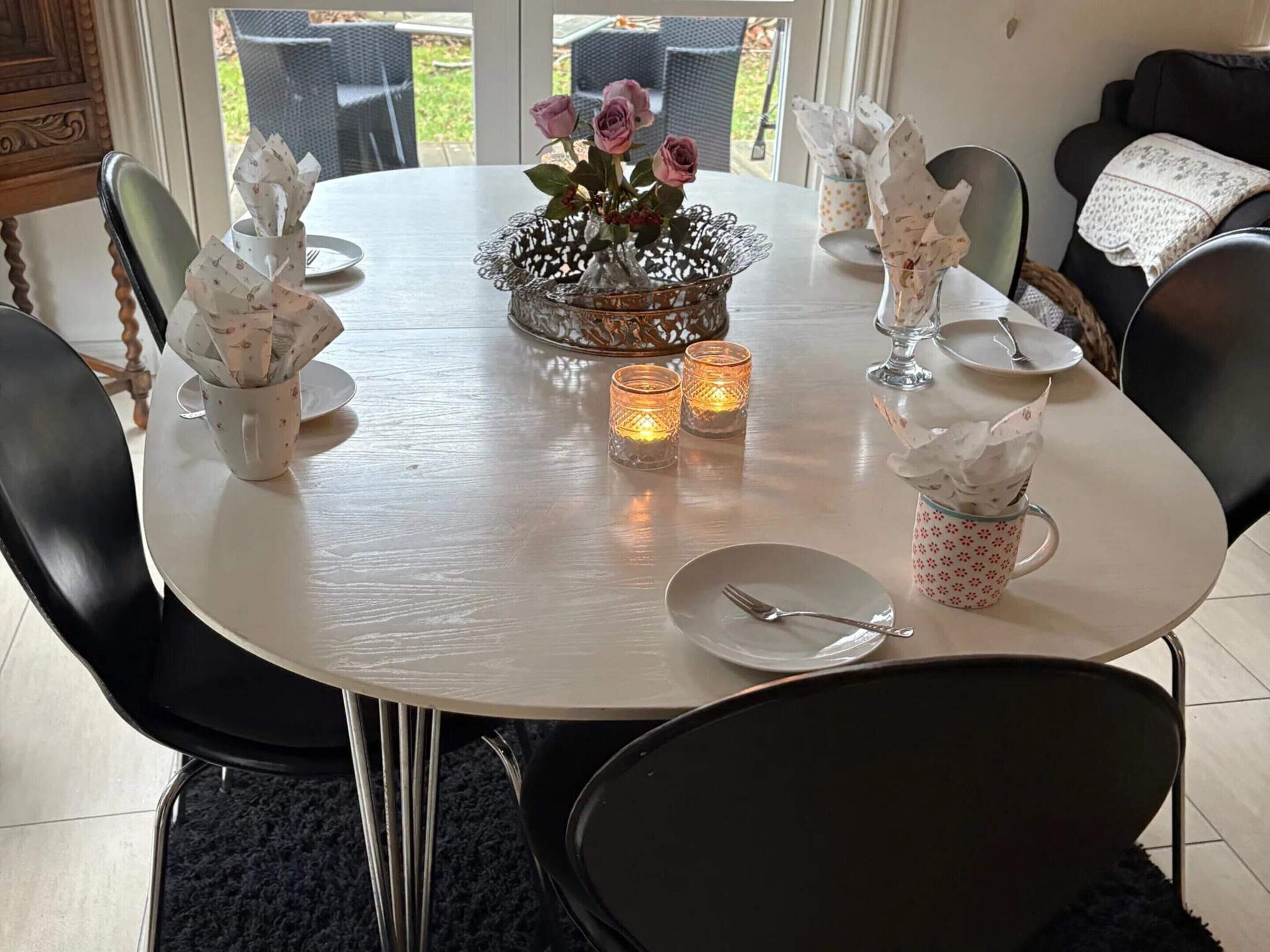 Mesa de jantar posta com xícaras de padrão floral, um vaso com rosas cor-de-rosa e castiçais.