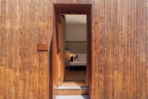 Uma porta de madeira que dá para um quarto com uma cama e uma parede branca.