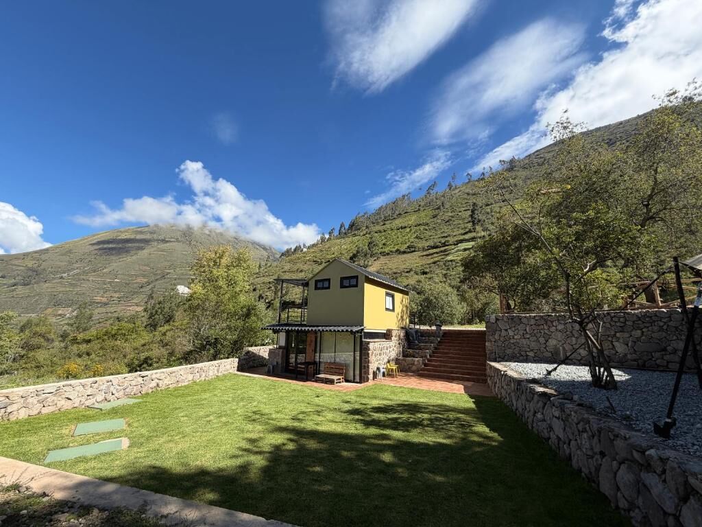 Um edifício amarelo com uma escadaria de pedra que leva a um terraço, cercado por um muro de pedra e uma área ajardinada.