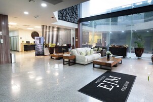 Um saguão de hotel com balcão de recepção, área de estar e uma grande janela de vidro.