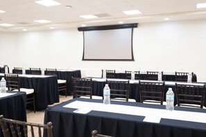 Sala de conferências com mesas, cadeiras e tela de projeção.