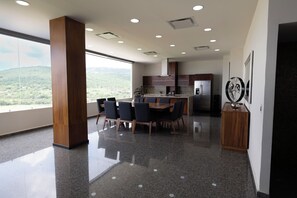 Uma cozinha moderna com uma ilha central, área de refeições com cadeiras e uma grande janela com vista para a paisagem.