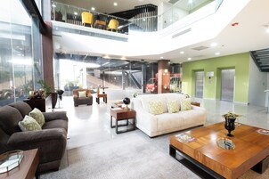 Um hall amplo com teto alto, área de estar com sofás e poltronas, mesa de centro e balcão de recepção.