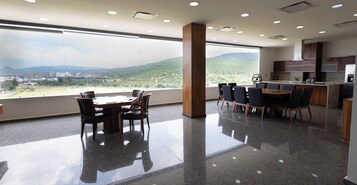 Quarto espaçoso com área de refeições, cozinha e uma grande janela com vista para uma paisagem montanhosa.