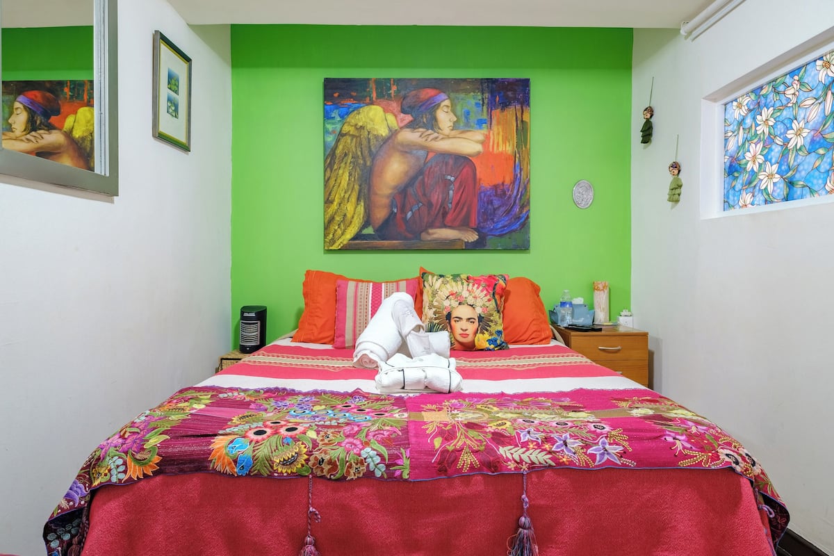 Um quarto com parede verde, uma cama com colcha florida e um quadro sobre a cama.