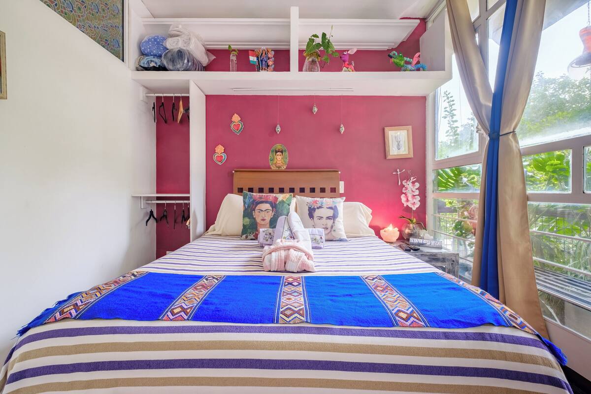 Uma cama com roupa de cama listrada, parede vermelha e janela com cortinas.