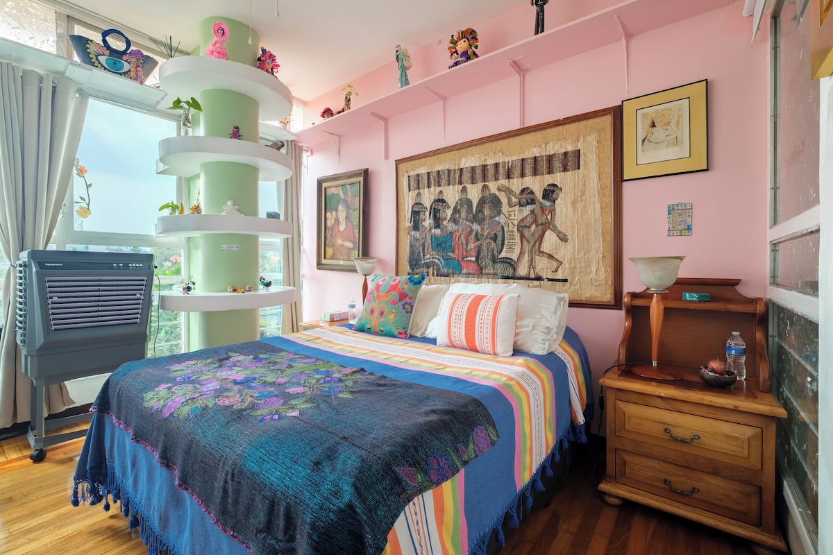 Quarto com uma cama, penteadeira, janela e parede decorada com obras de arte.