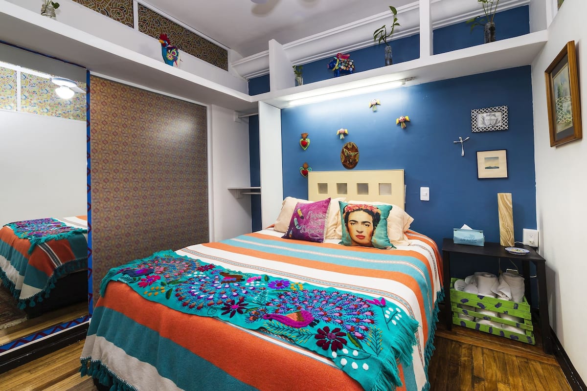 Quarto com cama, espelho, cômoda e parede azul decorada.