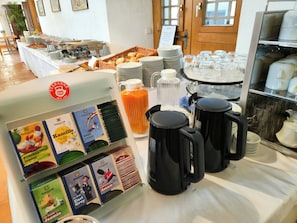 Disposição de buffet com diversos alimentos, máquinas de café e dispensadores de bebidas.