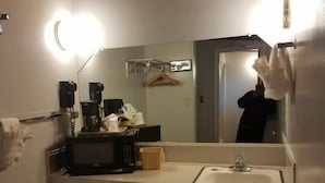 Casa de banho compacta com lavatório, espelho e micro-ondas sobre a bancada.