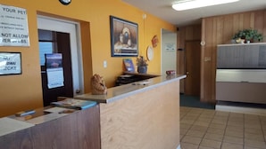 Uma receção com balcão de madeira, um quadro emoldurado acima e um aviso sobre taxas para animais de estimação.