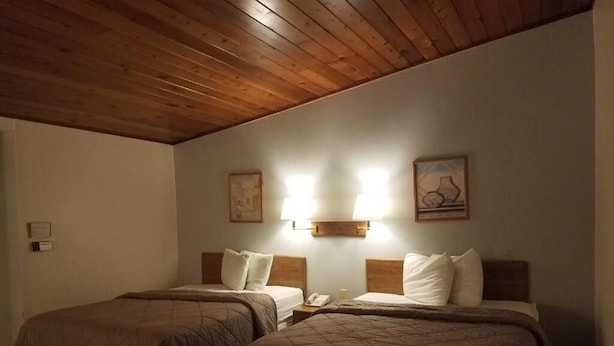 Quarto de hotel com duas camas, teto de madeira, luminárias fixadas na parede e quadros decorativos.