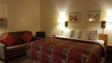 Quarto com cama, poltrona, sofá, duas luminárias na parede e um quadro emoldurado.