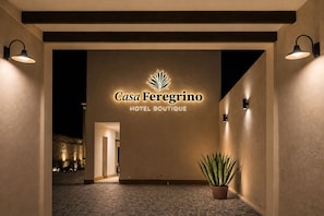 Entrada de hotel com uma placa indicando 'Casa Fergrino HOTEL BOUTIQUE', uma planta em vaso e um caminho de pedras.