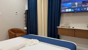 Quarto de hotel com uma cama, uma cadeira, televisão fixada na parede e um armário de madeira.