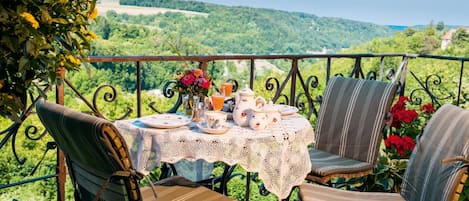 Uma área de refeições ao ar livre com uma mesa posta para dois, rodeada por cadeiras, com vista para uma paisagem deslumbrante.