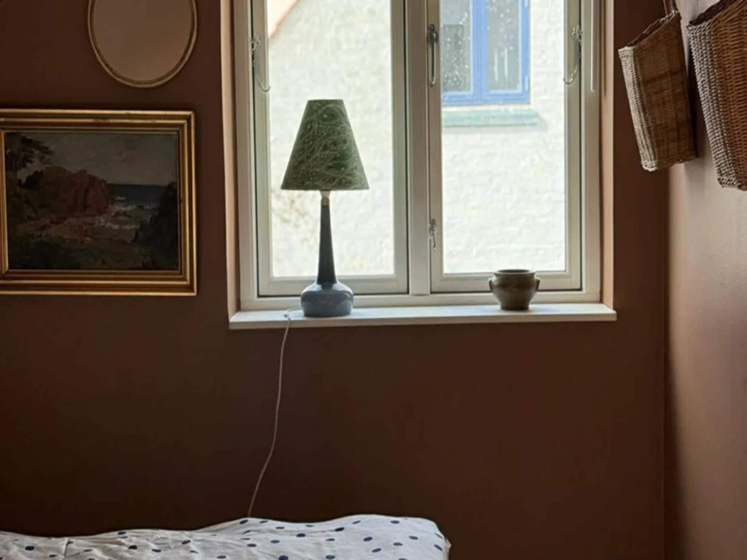 Quarto com cama, janela com vista, luminária e pintura na parede.