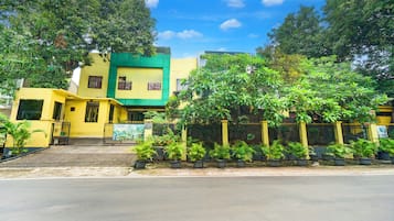 Um edifício de vários andares com fachada verde e amarela, rodeado por vasos de plantas e árvores.