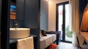 Quarto de hotel moderno com uma pia grande, uma cama com almofadas, uma cadeira e vista para o exterior.