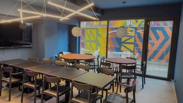 Uma sala de conferências moderna com mesas, cadeiras, uma tela grande e arte abstrata geométrica nas paredes.