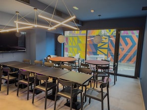 Uma sala de conferências moderna com mesas, cadeiras, uma tela grande e arte abstrata geométrica nas paredes.