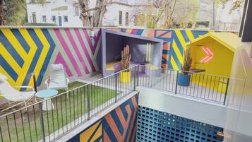 Uma área externa com vários níveis, apresentando designs geométricos coloridos na parede, assentos e plantas em vasos.