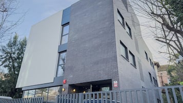Um edifício moderno com fachada cinzenta, janelas amplas e sinalização visível de alarme de incêndio.