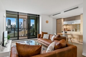 Uma sala de estar moderna com um sofá, uma mesa de centro e vista para a cidade através de janelas amplas.