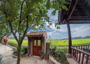 Uma casa rústica de tijolos com telhado de cerâmica, porta de madeira e um pequeno alpendre com corrimão.