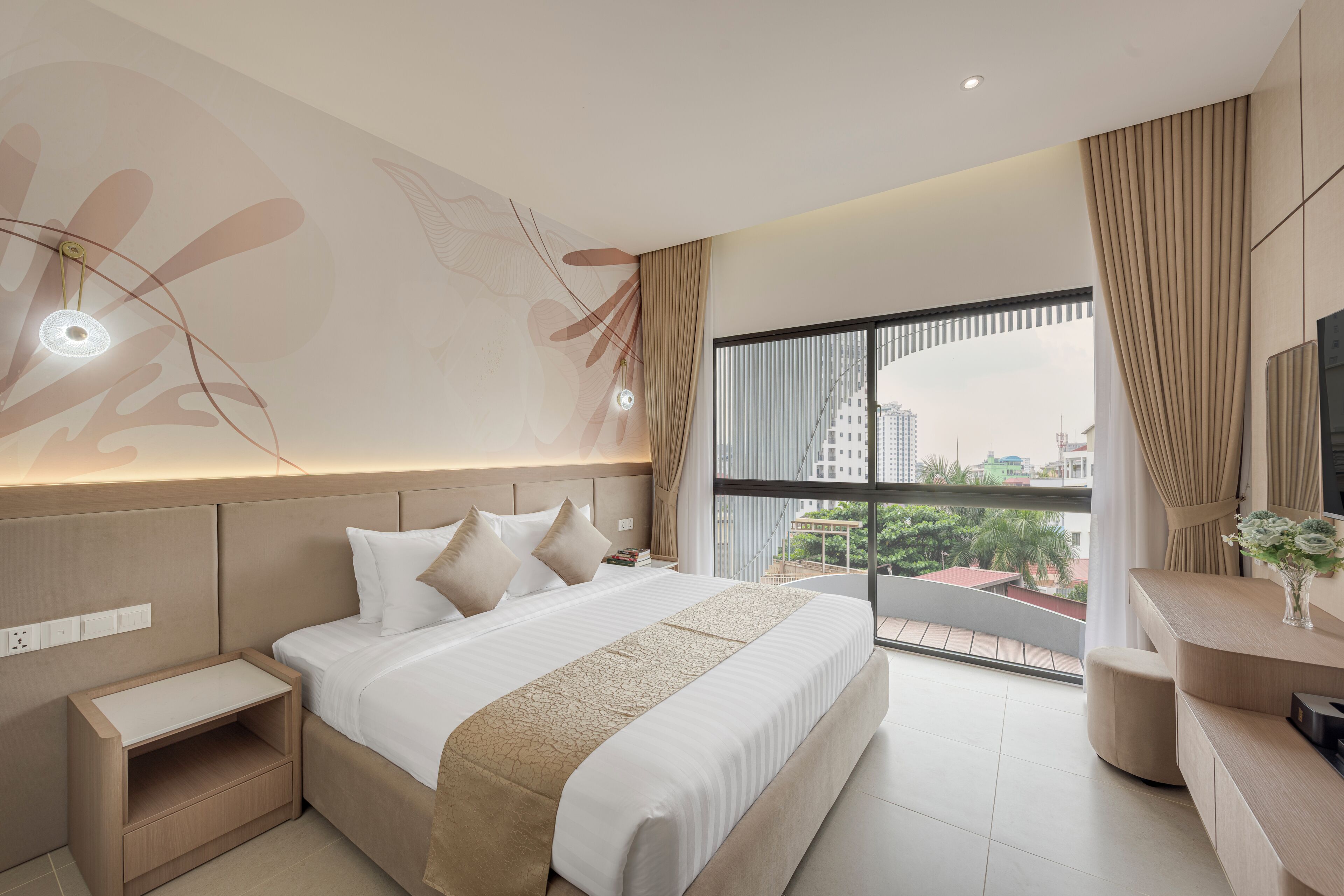 Quarto de hotel moderno com uma cama grande, mesas de cabeceira, escrivaninha e vista para a cidade.