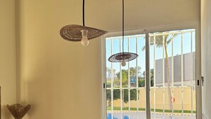 Quarto com sofá, pequena cozinha com pia, janela com vista para piscina e palmeiras, e luminárias pendentes.