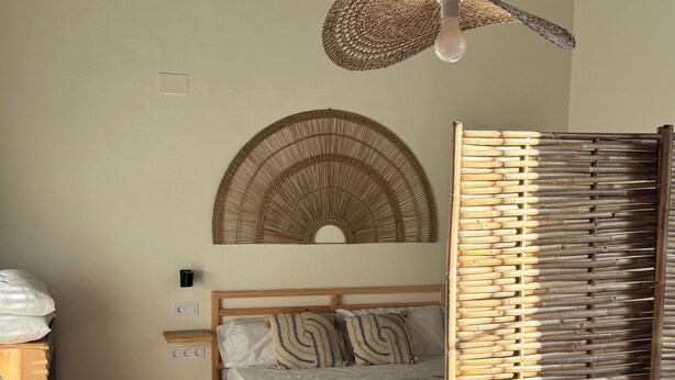 Quarto com cama, mesa, cadeiras, luminária pendente e decoração de parede em tecido.
