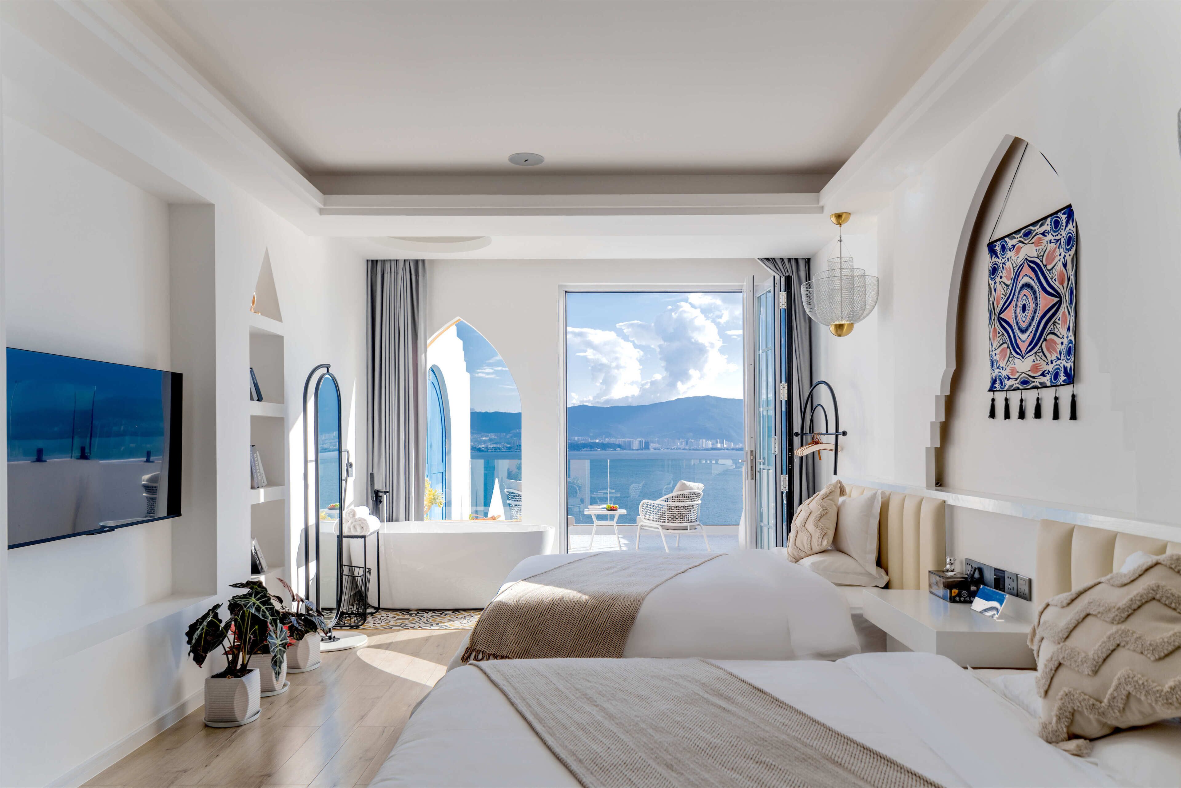 Quarto de hotel moderno com uma cama grande, um sofá, uma TV e uma varanda com vista para o mar.