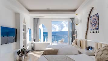 Quarto de hotel moderno com uma cama grande, um sofá, uma TV e uma varanda com vista para o mar.