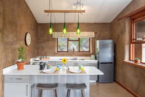 Uma cozinha moderna com ilha central, banquetas, geladeira e janela com vista para o verde.