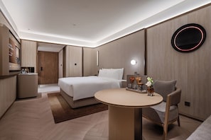 Quarto de hotel moderno com cama, mesa de cabeceira, cadeira e uma mesa redonda com um vaso de flores.