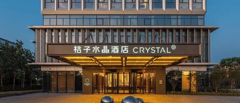 Uma entrada de hotel moderna com uma placa indicando 'Crystal Hotel', fachada de vidro e um espelho d'água à frente.